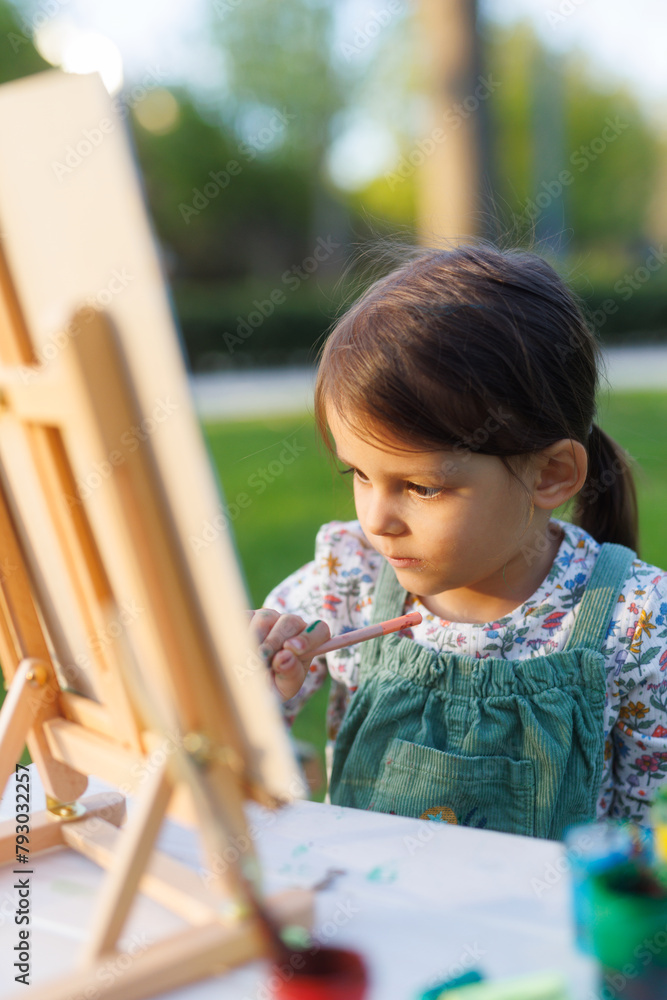 Little girl is painting a picture in the park on the green grass. Child ...