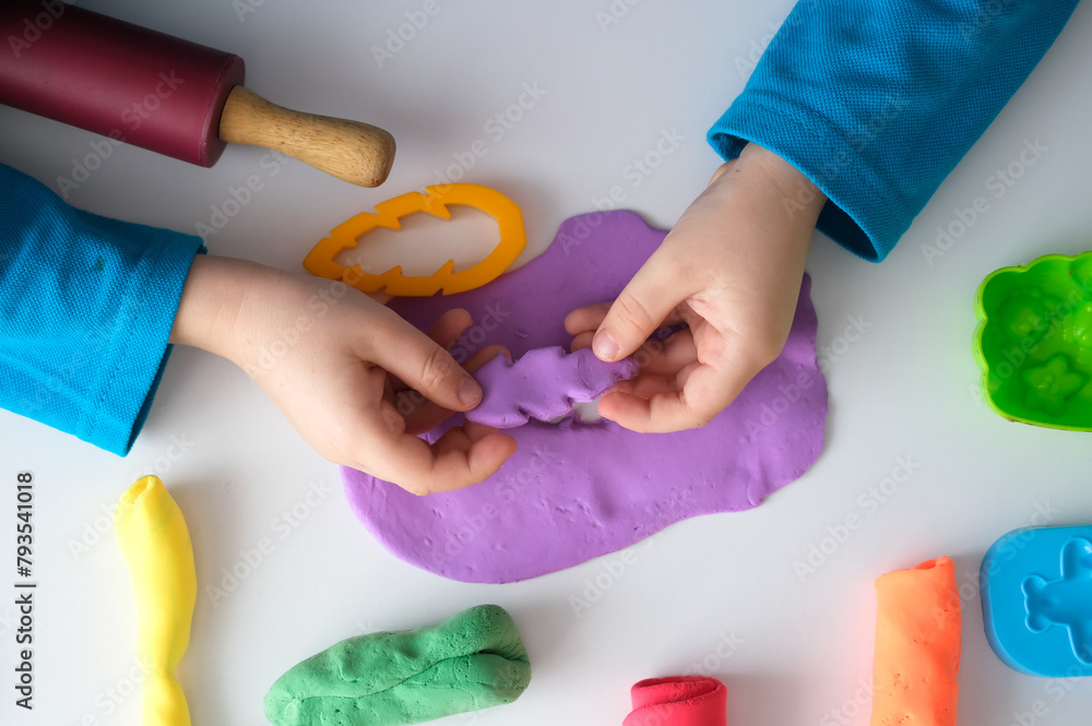 Child's hands make flower and other things from multi-colored clay ...