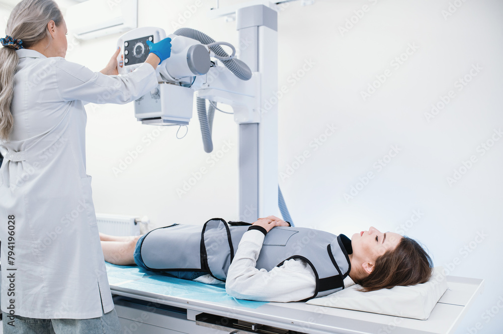Female patient lying on bed while female nurse adjusting modern X-ray ...