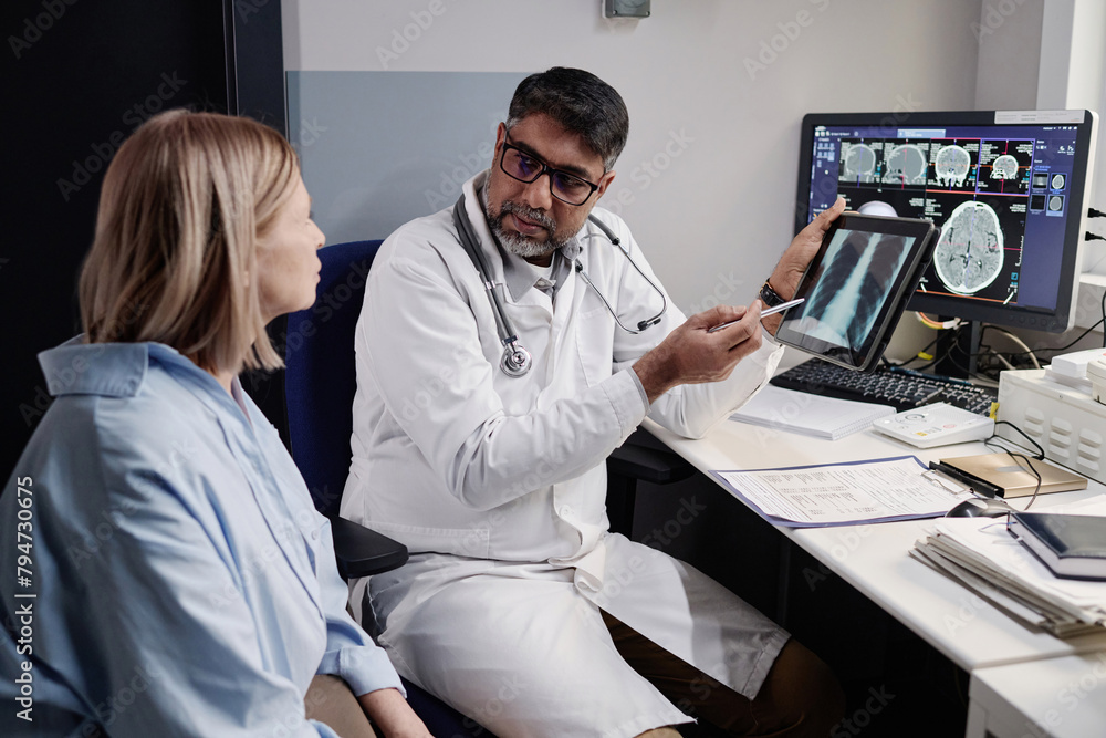Serious biracial radiographer showing chest X-ray image to mature ...