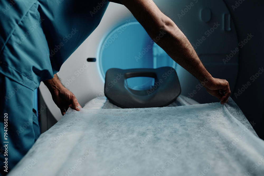 Unrecognizable male radiographer preparing CT scanner bed covering it ...