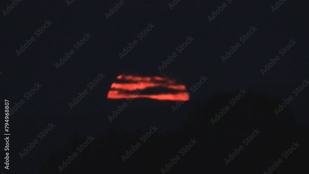 Red full moon rising from behind black horizon with forest and between ...