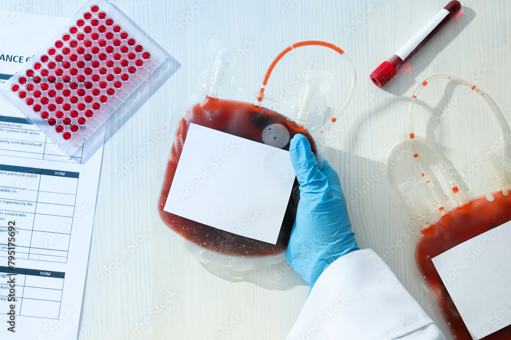 Bags and test tube with donor blood, documents and gloved hand on light ...