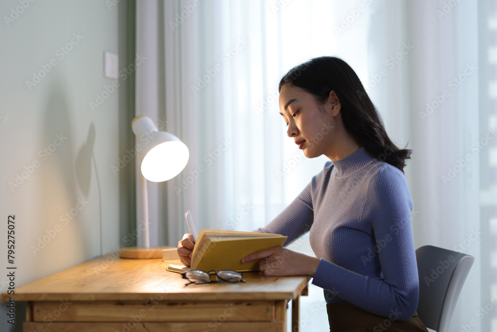 Beautiful young Asian woman is writing a diary on the table at home ...
