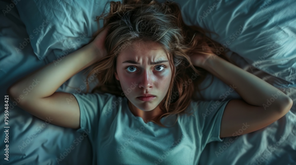 Overhead shot of a terrified young woman in bed, gripping her head in ...