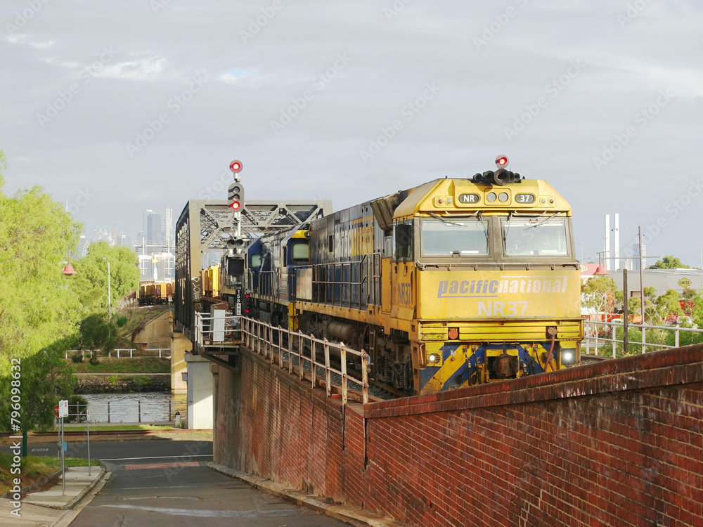 A Pacific National train passing a steel bridge over Maribyrnong River ...