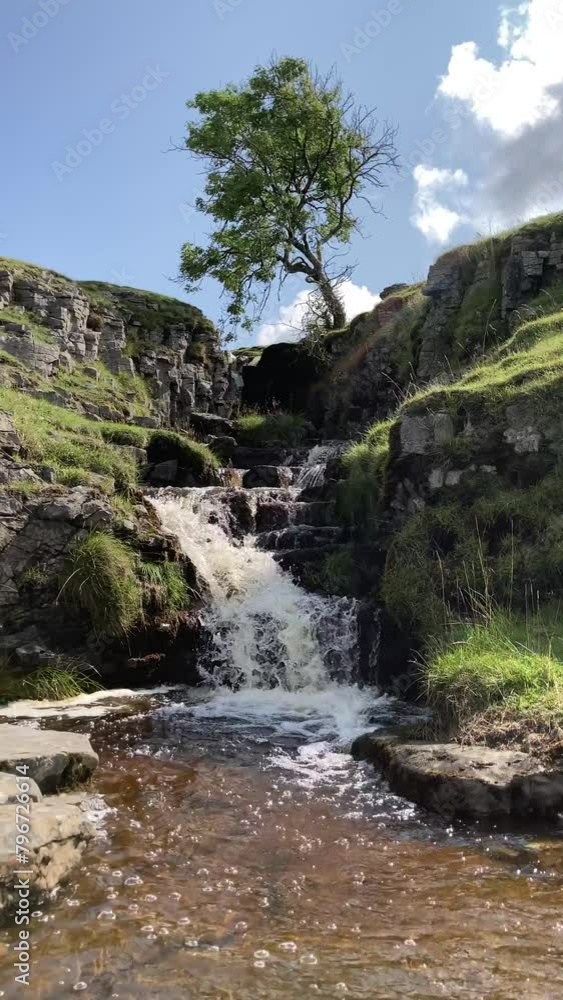 A scenic waterfall cascades over limestone rocks into a stream with a ...
