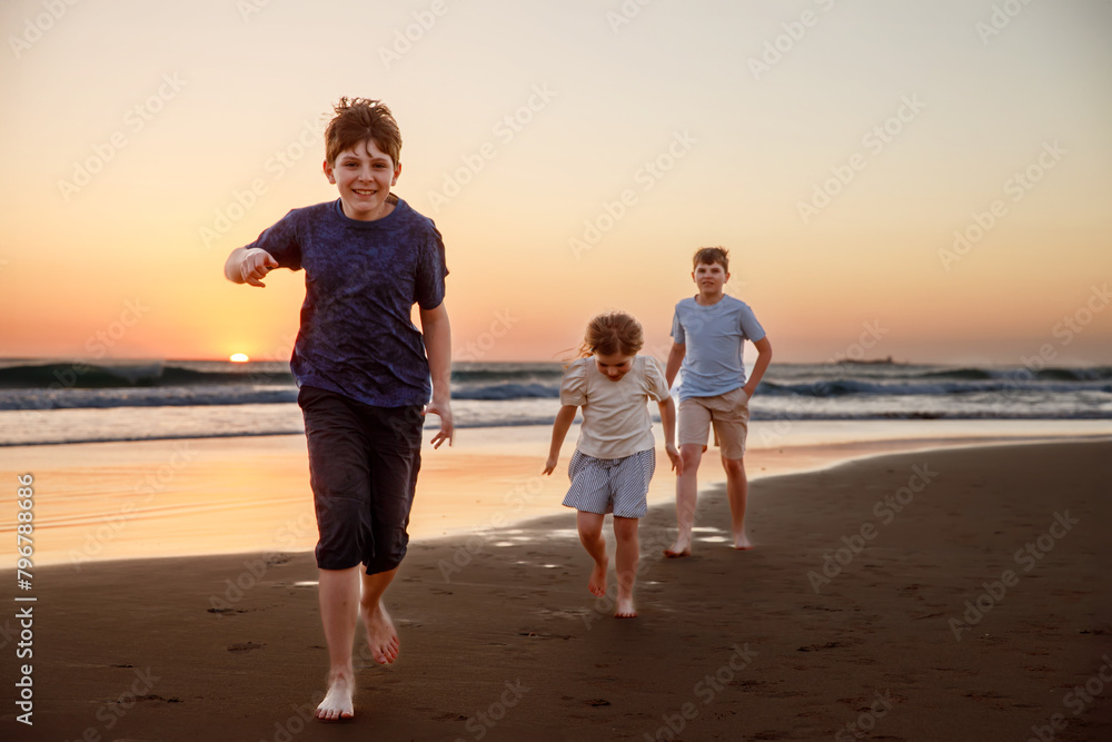 Three kids silhouettes running and jumping on beach at sunset. happy ...