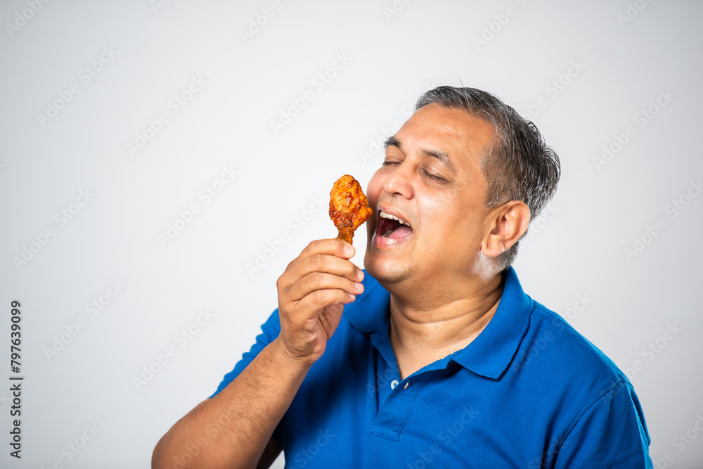 Indian asian mid age handsome man eating chicken leg piece with ...