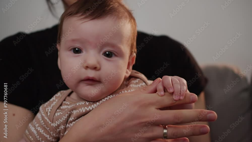 Close up a little girl a baby in a brown T-shirt sits in the arms of ...