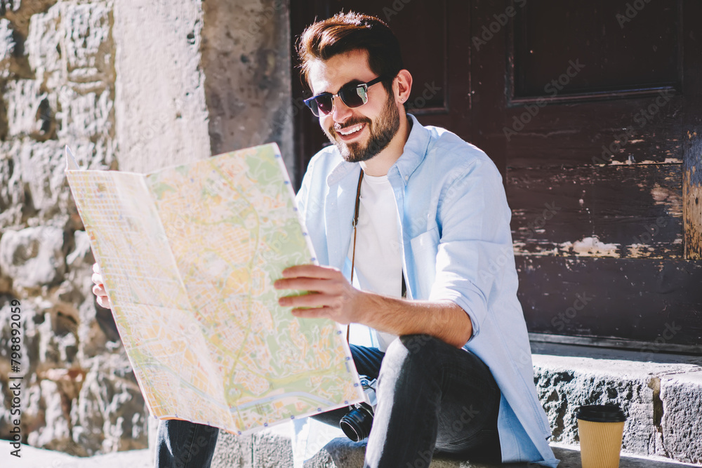Happy stylish young man reading map with interesting showplaces and to ...