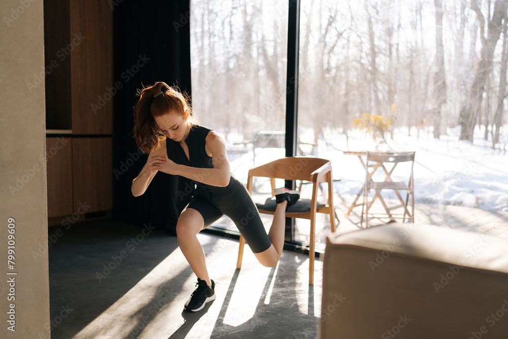 Sportive slim female doing single leg lunge using chair in living room ...