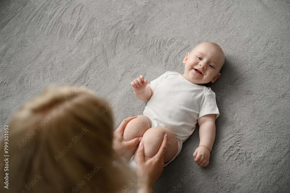 Mom does gymnastics to newborn baby on bed at home, bending her legs ...