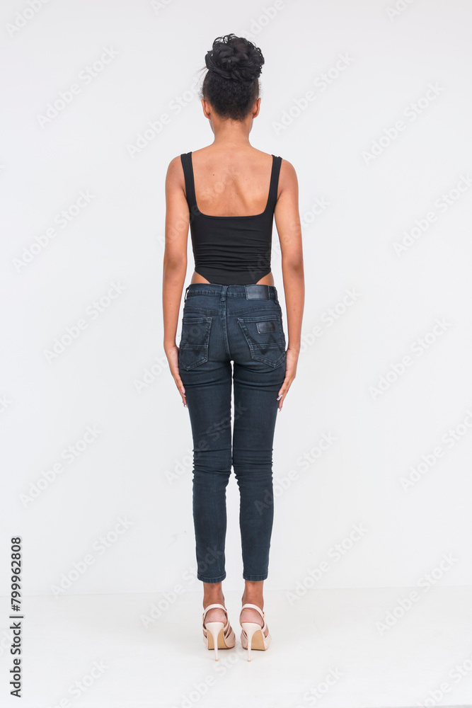 Elegant woman in black bodysuit and jeans posing from behind, white ...