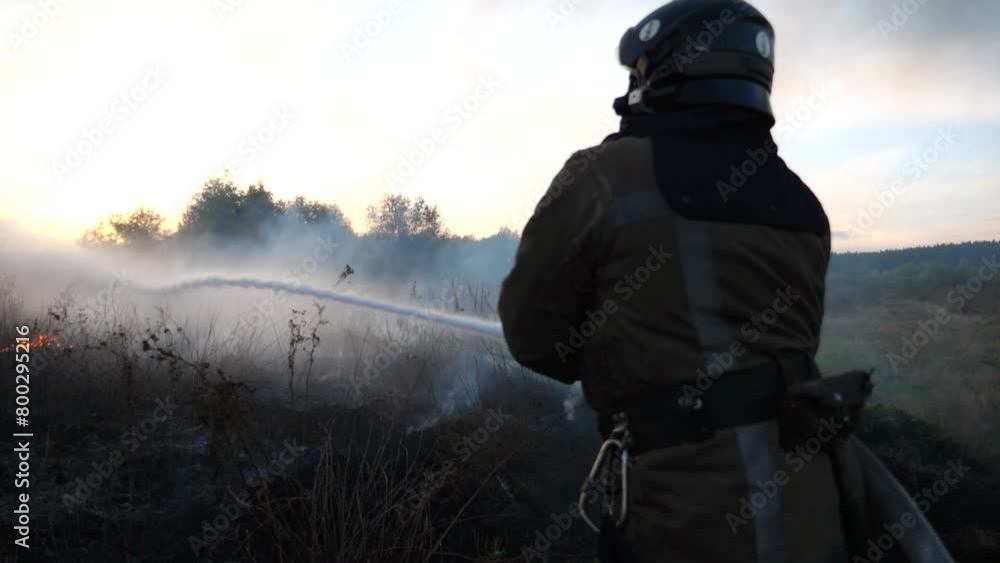 Male firefighter in uniform extinguishes burning dry grass using fire ...