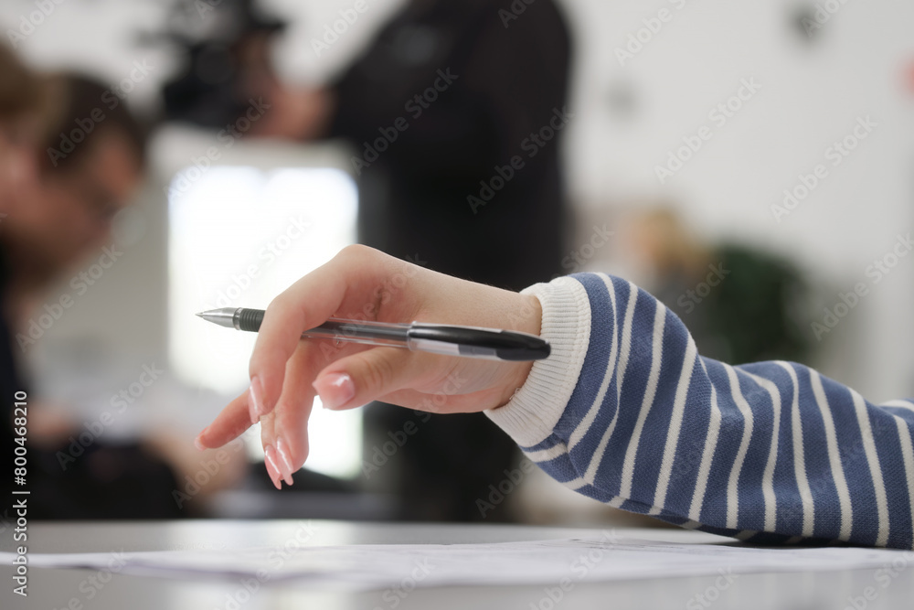 Female student holding a pen in her hand, sitting at a desk in a ...