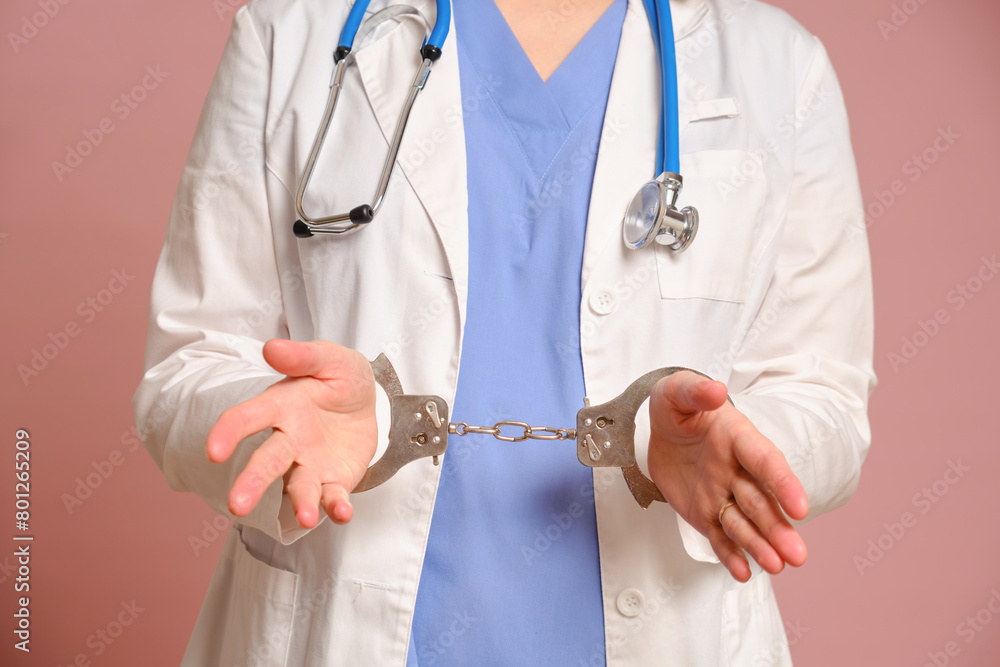 Female doctor with hands handcuffed during arrest, studio pink ...