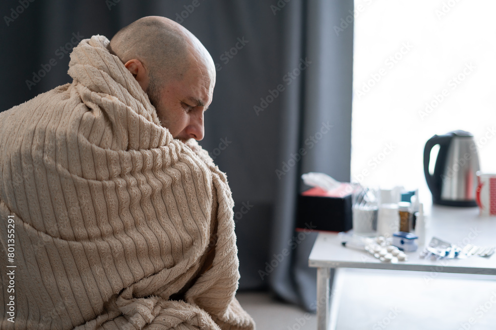 Bearded sick sad man wrapping blanket sits on couch suffers from flu ...