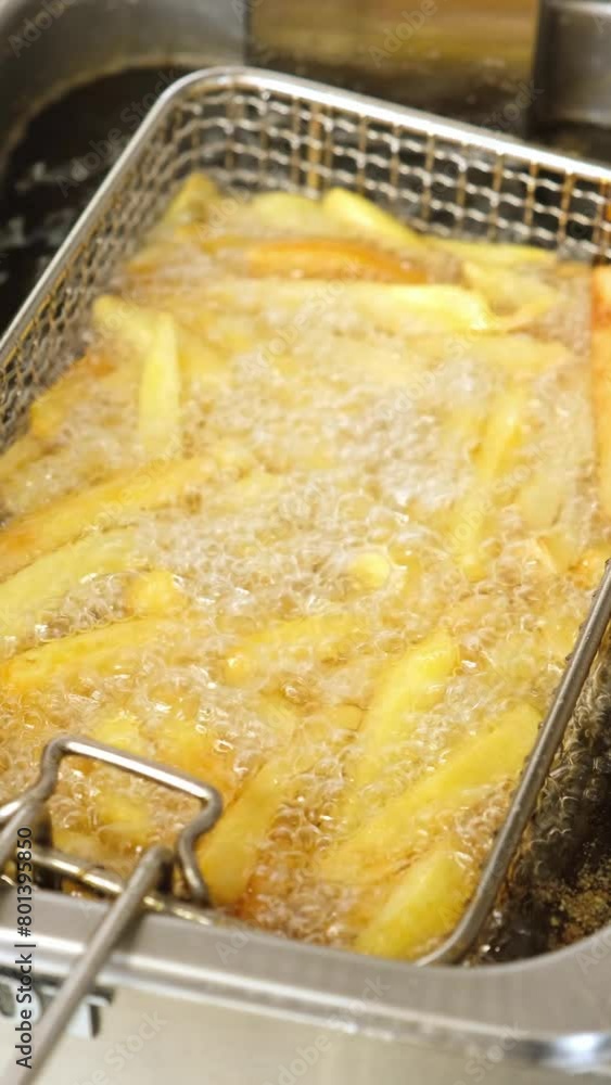 Close up of french fries is cooking into deep fryer. Crunchy potatoes is frying in hot boiling ...