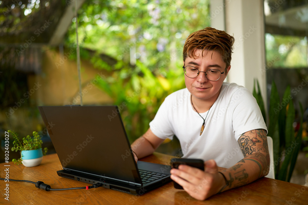 Transgender office worker with tattoos checks smartphone, distracted ...