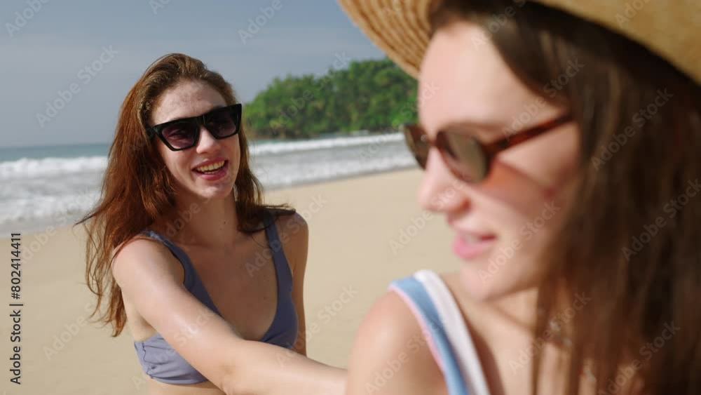 Happy young woman applying sunscreen on friend's back at sandy beach ...