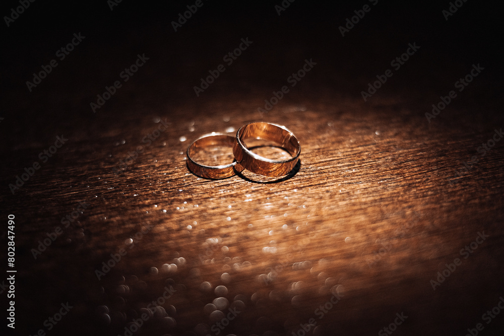 Two gold wedding rings are placed on a wooden surface. The rings are ...