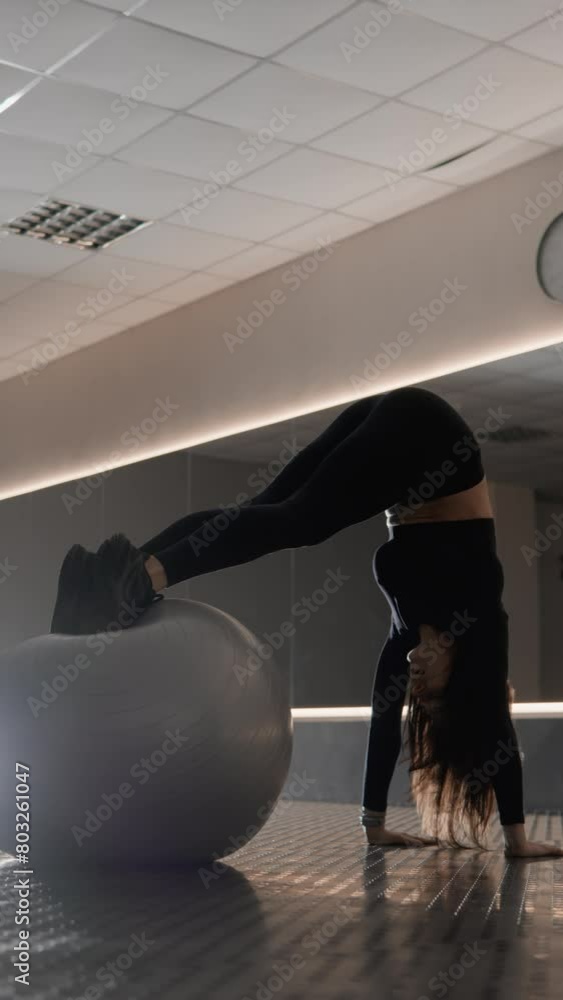 A woman in a fitness room performs fitball exercises with impressive skill and flexibility. Her ...