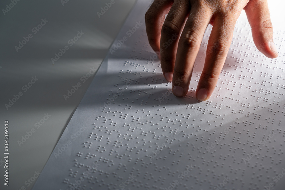 Hand of a blind person reading some braille text on page paper to learn ...