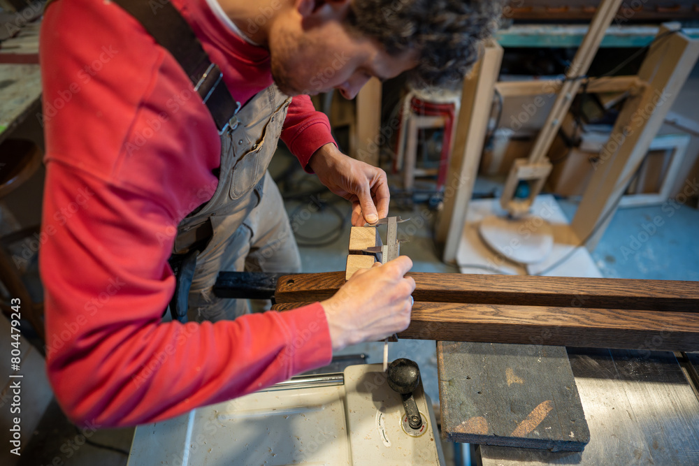 Focused male carpenter with precision measures DIY wooden bed legs with ...