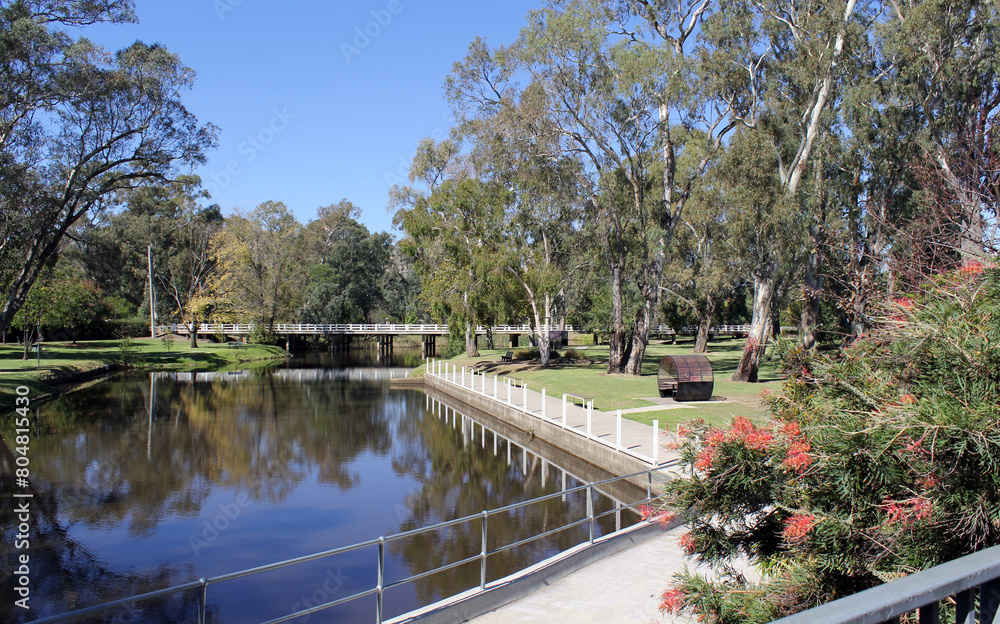 Water and bridge surrounded by grass, trees, and flowering shrubs at ...