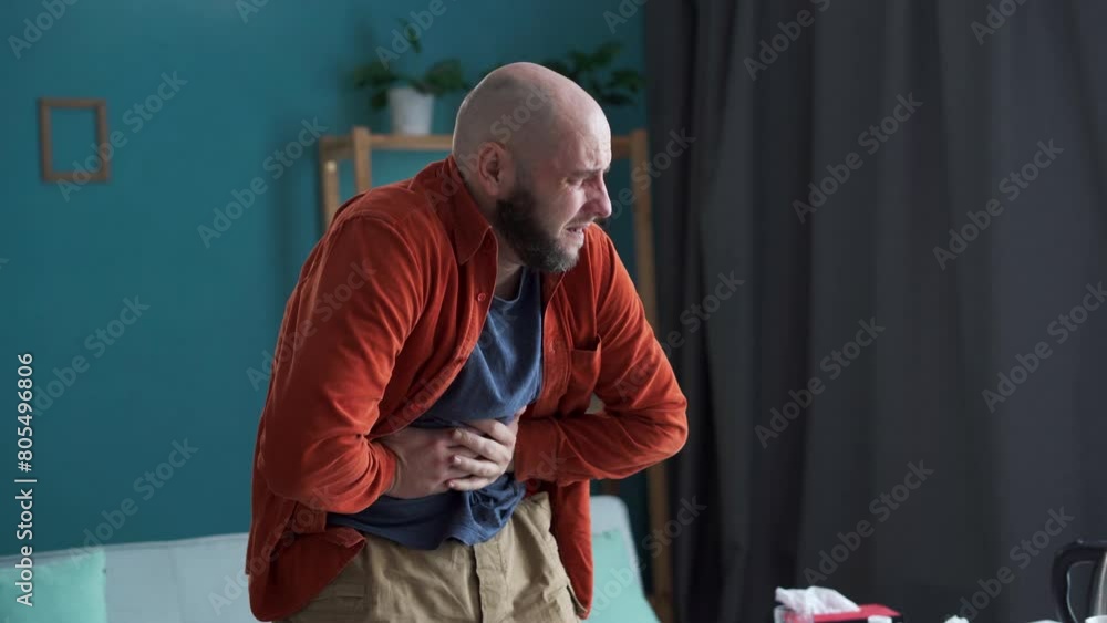 Bearded man suffering with severe stomach pain at home. Male hands ...