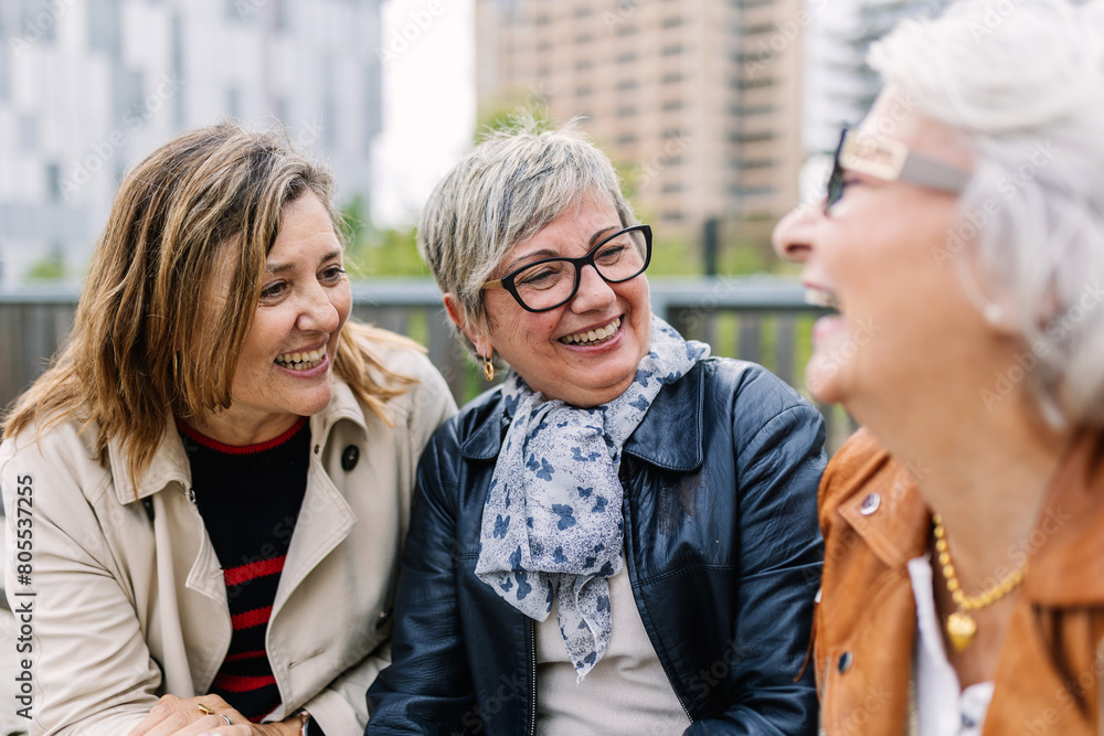 Three mature retired women laughing while talking sitting outside ...