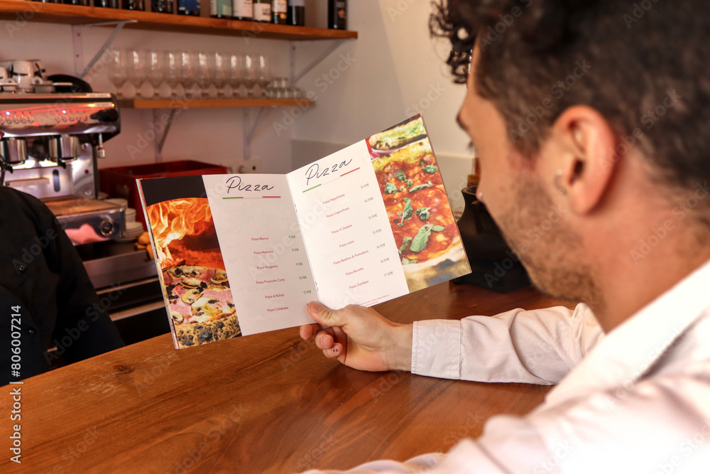Person choosing food from a menu seen from behind in a pizza restaurant ...