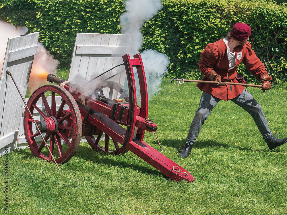 a red cannon is firing, smoke after the salvo, a man in a historical ...