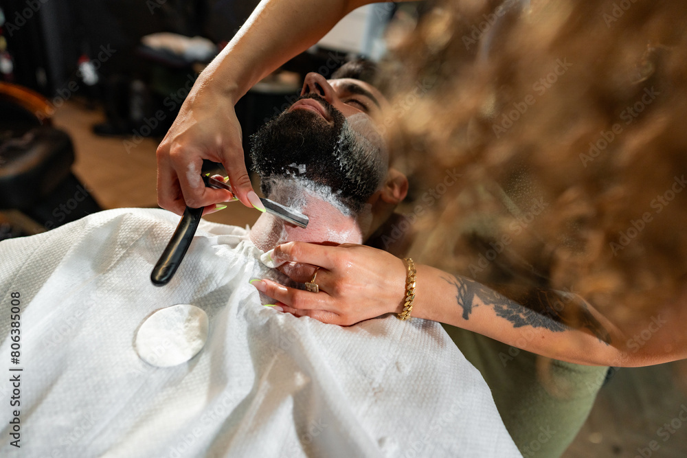 Barber carefully shaves under the neck with a straight razor, focusing ...