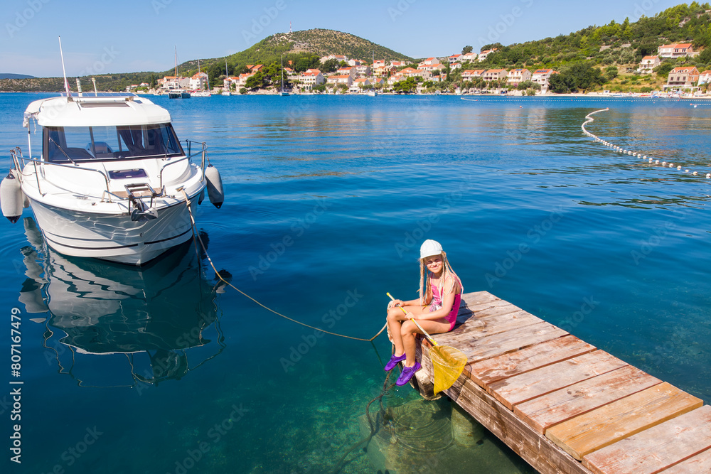 Cute little girl kid sits on wooden pier next moored boat yacht with ...