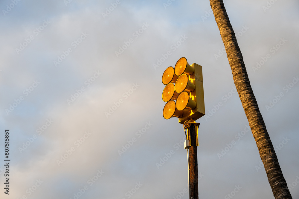 Bright yellow tsunami sirens and palm trees against a cloudy sky at ...