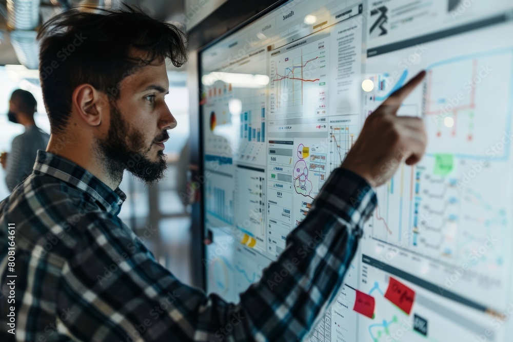 A man stands pointing to a digital whiteboard filled with flowcharts, graphs, and bullet points ...