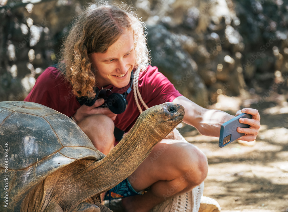 Smiling tourist boy making a selfie using cell phone with Aldabra giant ...