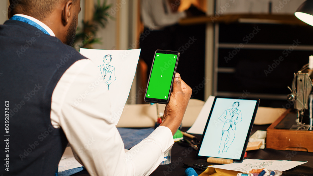 Tailor using greenscreen in atelier with team of designers, looking at ...