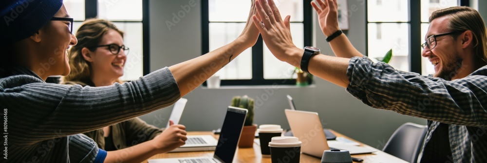 Four colleagues in a bright office engaging in a high five, depicting ...