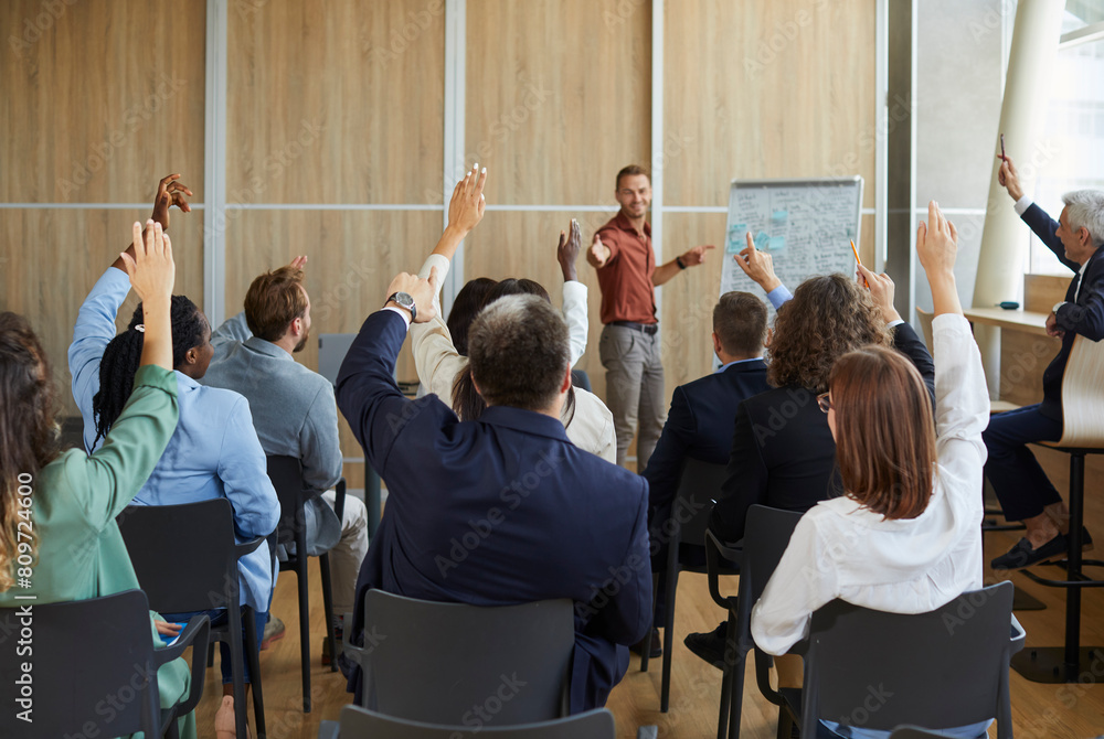 Young colleagues raising hands to ask questions during business meeting ...