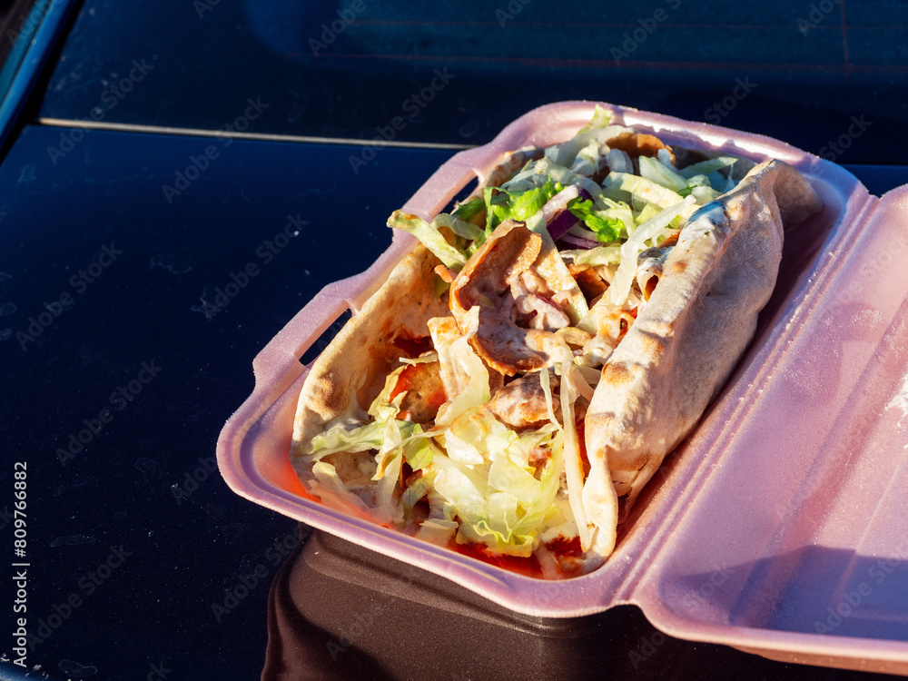 Chicken kebab wrap meal in a plastic pink container on blue car trunk ...