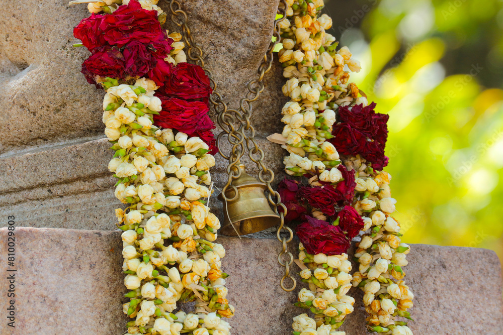 A flower garland and a bronze bell on a temple sculpture in India ...