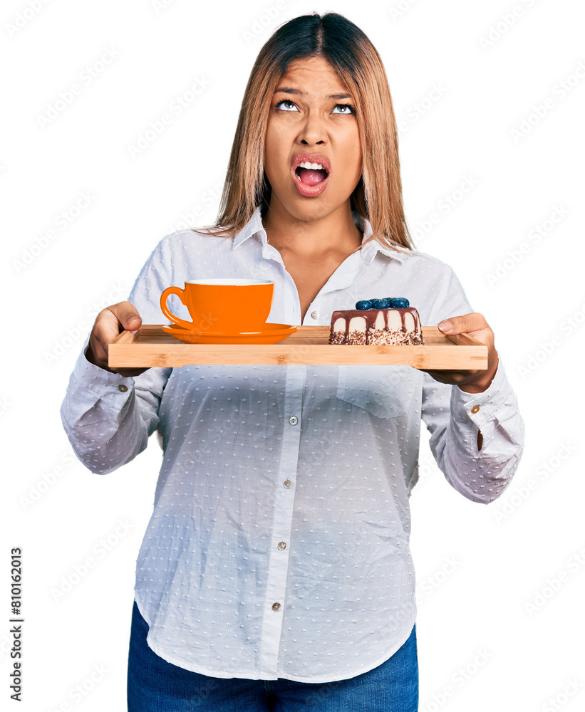 Young hispanic woman holding tray with coffee and cake angry and mad ...