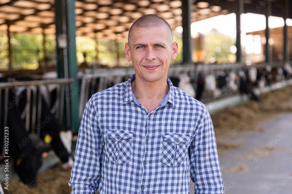 Successful young man owner of dairy farm standing in stall on ...