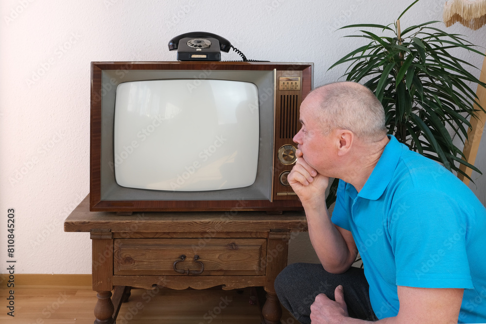 elderly man in blue polo shirt sits on floor in front old retro analog ...
