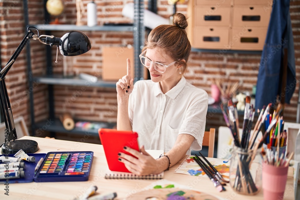 Excited young blonde artist in studio, joyfully pointing at tablet ...