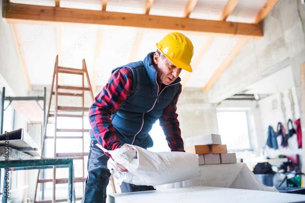 Older worker carrying heavy bag with building material. Work injury ...