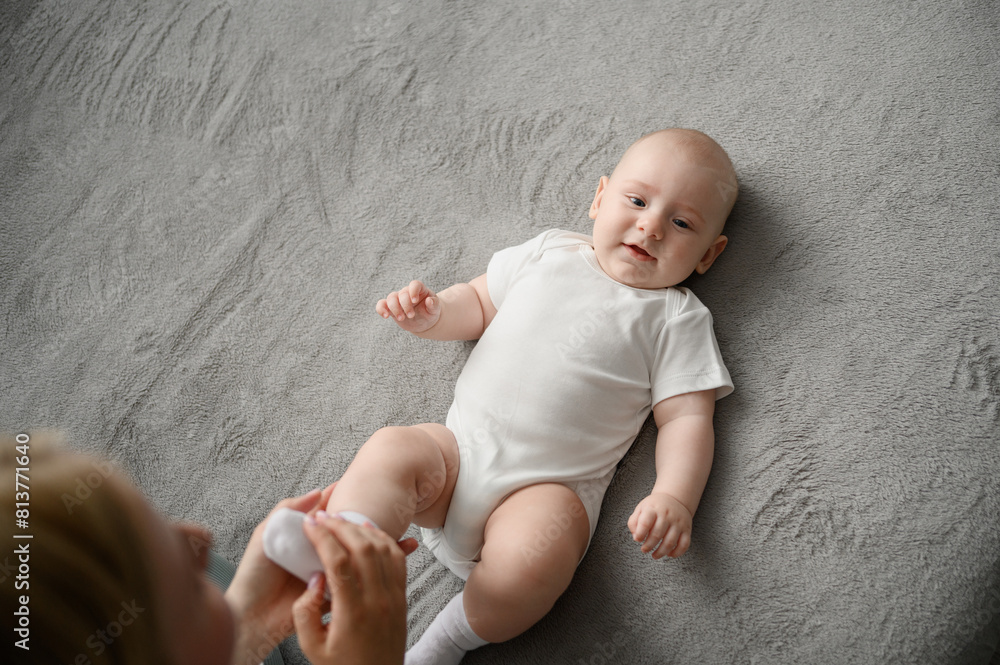 Baby lies on bed after waking up, mother tickles the infanta heel. Mom ...